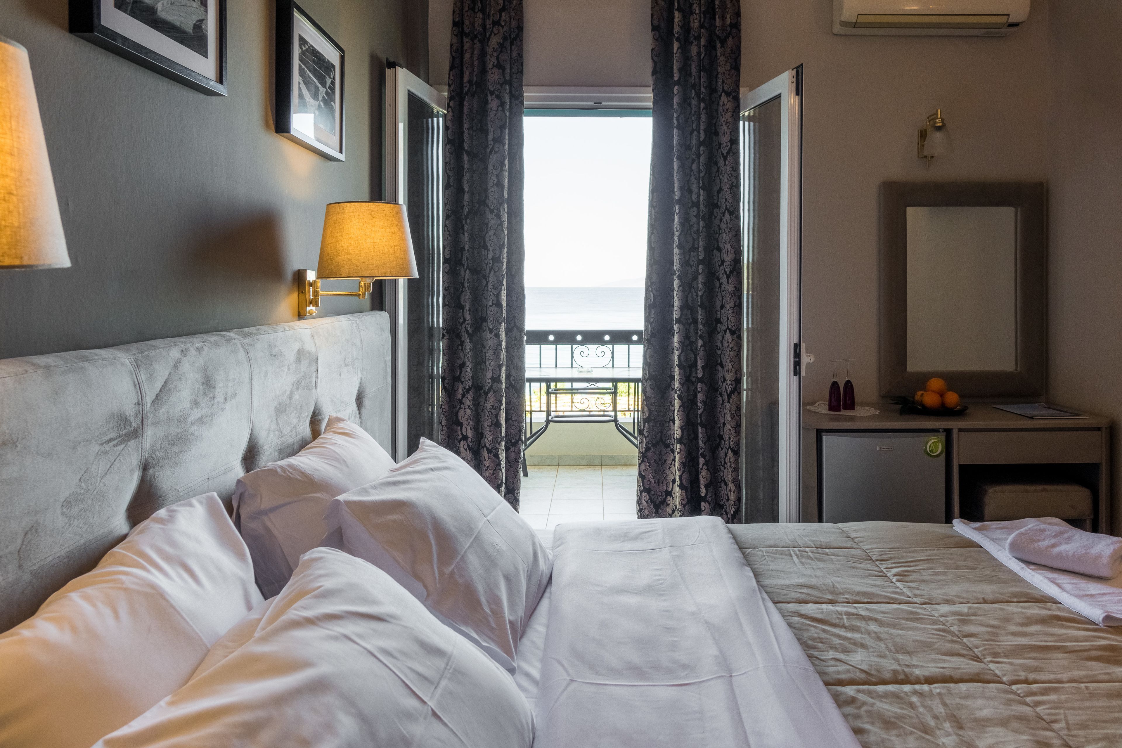 Quarto de hotel com uma cama, uma mesa de cabeceira com abajur, uma pequena escrivaninha com espelho e vista para a varanda.