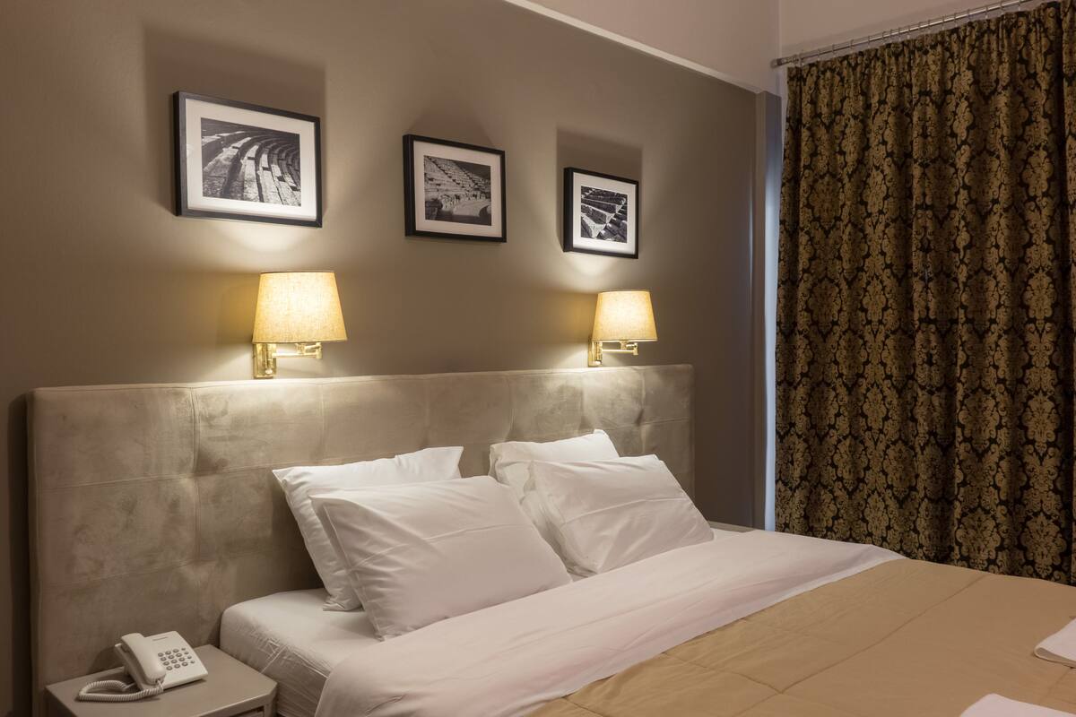 Quarto de hotel com cama, duas luminárias de cabeceira, telefone e três quadros na parede.