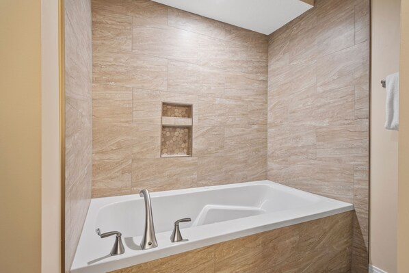Um banheiro moderno com uma banheira independente, uma estante embutida com objetos decorativos e um porta-toalhas.