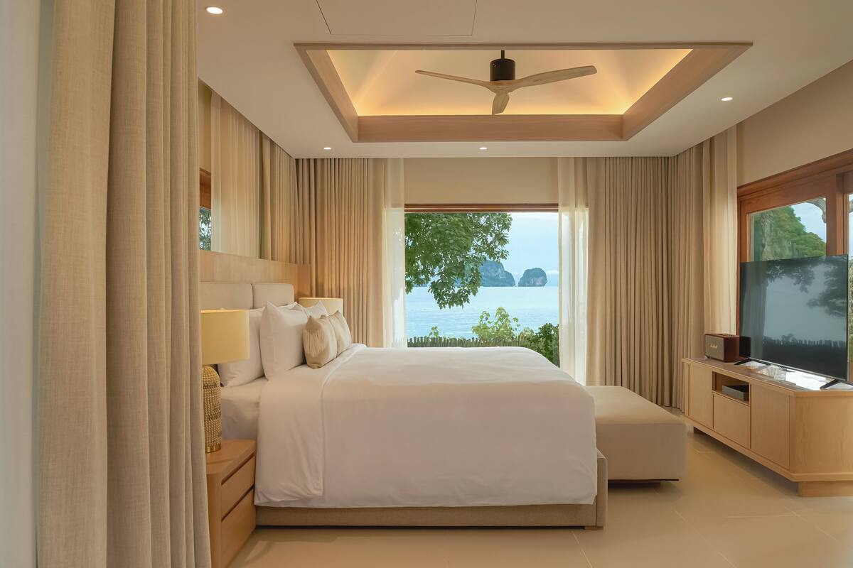 Quarto moderno com uma cama grande, televisão e vista para o mar.