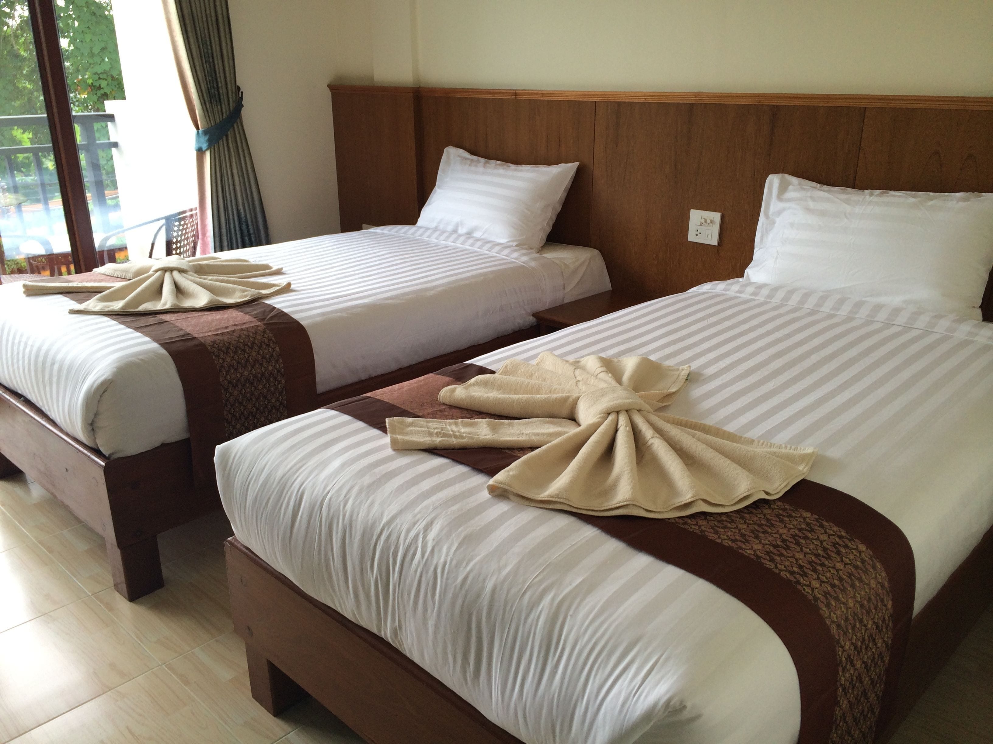 Duas camas de casal com cabeceiras de madeira, roupa de cama branca e toalhas bege dispostas sobre as camas.