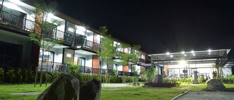 Um hotel com vários andares, varandas, uma entrada bem iluminada e um jardim ajardinado.