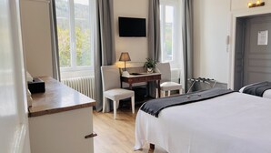 Quarto de hotel com cama, escrivaninha, cadeira e televisão na parede.