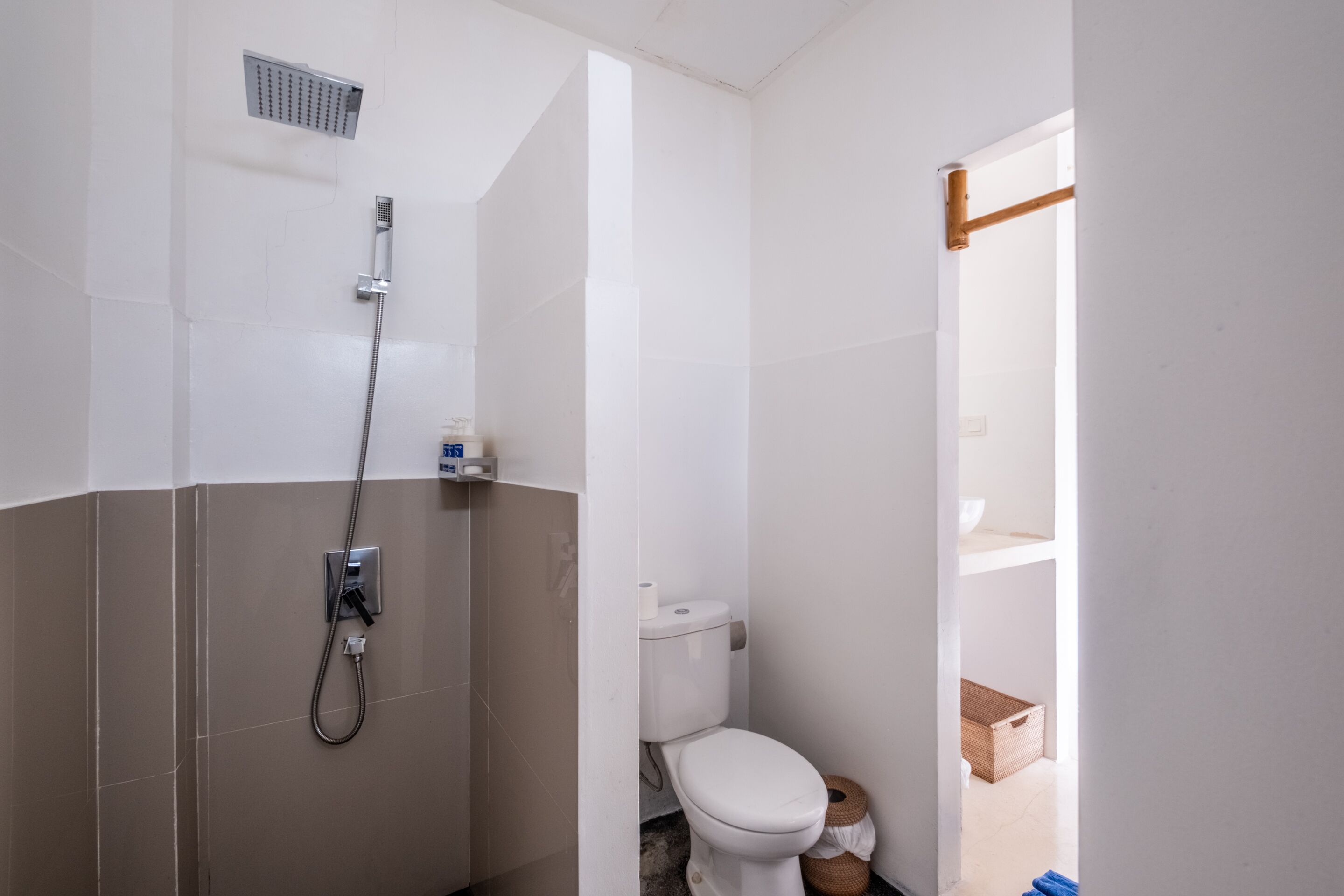 Casa de banho pequena e limpa, com chuveiro, sanita e área de arrumação visível com cestos.