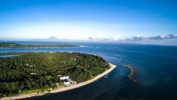 Vista aérea de uma área costeira com uma península arborizada, uma praia e montanhas ao longe.
