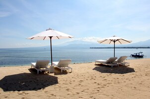 Na praia, areia branca, espreguiçadeiras, guarda-sóis