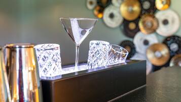 Uma área de bar com uma taça de martini, um copo de cristal e um recipiente de metal.