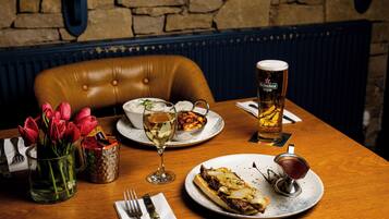 Uma mesa de jantar com uma refeição, um copo de cerveja e um vaso de tulipas vermelhas.
