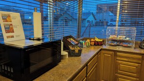 Uma bancada de cozinha com micro-ondas, uma cesta de frutas e uma seleção de lanches embalados.