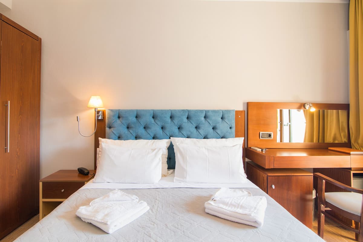 Quarto de hotel com uma cama, uma mesinha de cabeceira de madeira, uma escrivaninha e uma cadeira.