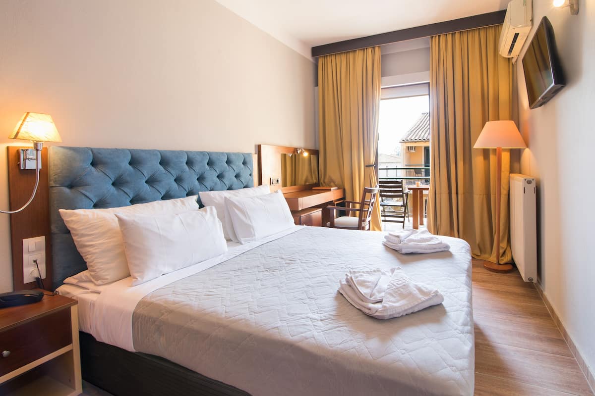 Quarto de hotel com uma cama grande, uma escrivaninha, uma cadeira, uma TV e uma varanda com cortinas.