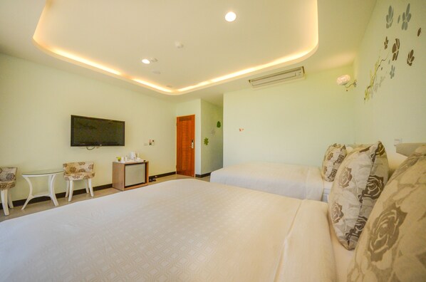 Quarto de hotel com uma cama grande, duas camas menores, uma televisão na parede, uma mesa com cadeira e uma porta que dá para outro quarto.
