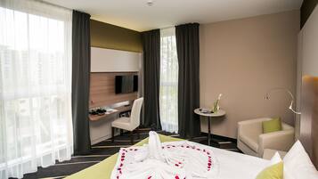 Quarto de hotel com cama, escrivaninha, cadeira, mesa pequena e sofá.