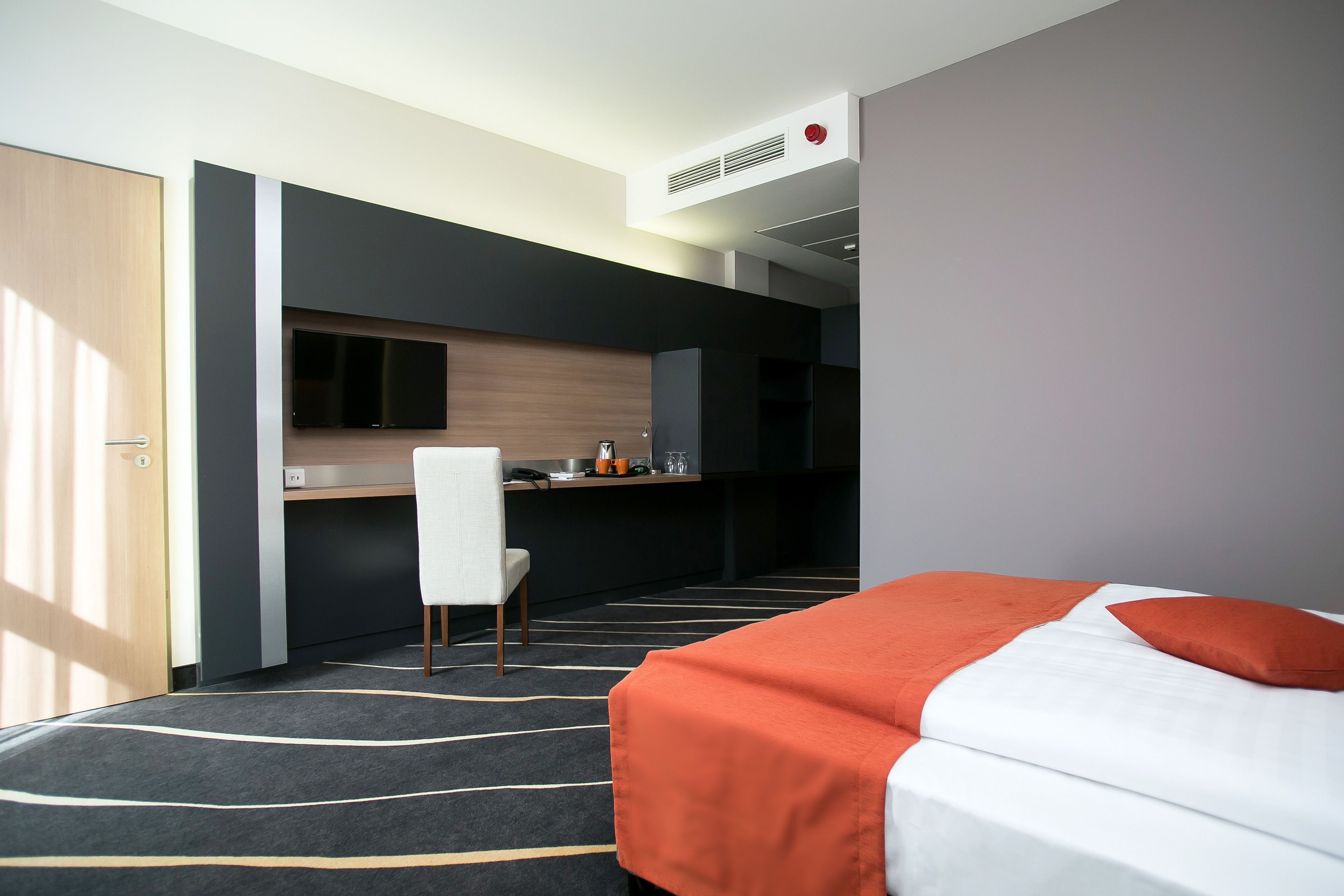 Quarto de hotel com cama, escrivaninha, cadeira e televisão.