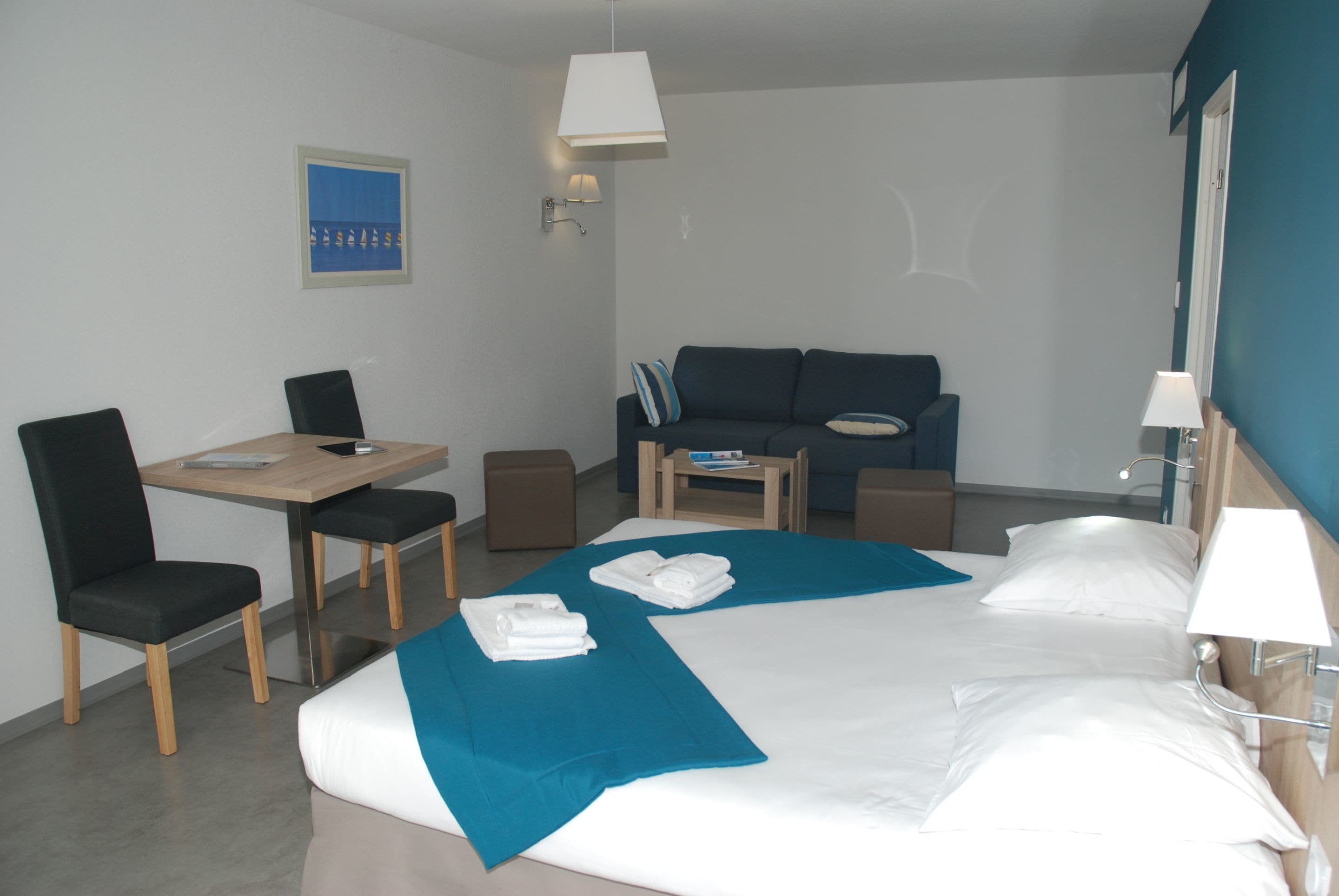 Quarto de hotel com cama, escrivaninha, cadeira, sofá e mesa pequena.