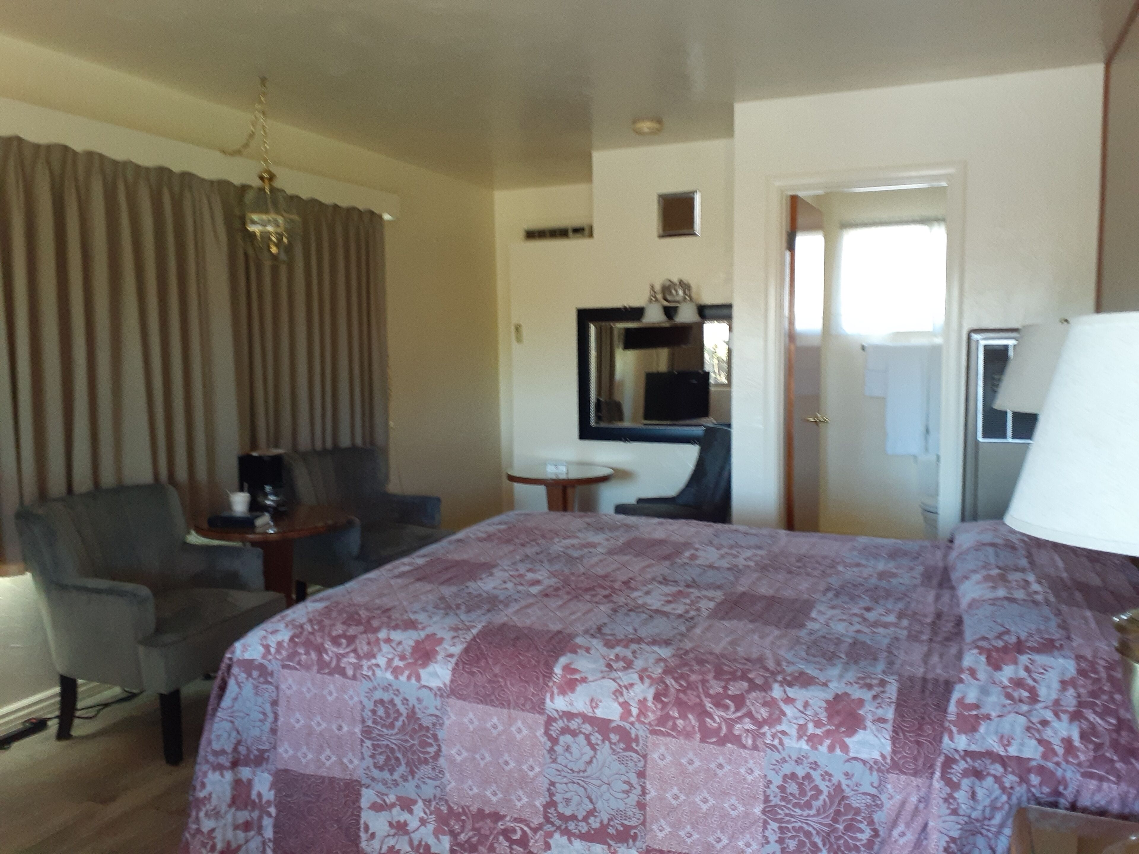 Quarto de hotel com uma cama grande, uma escrivaninha, uma cadeira, uma televisão e uma janela com cortinas.