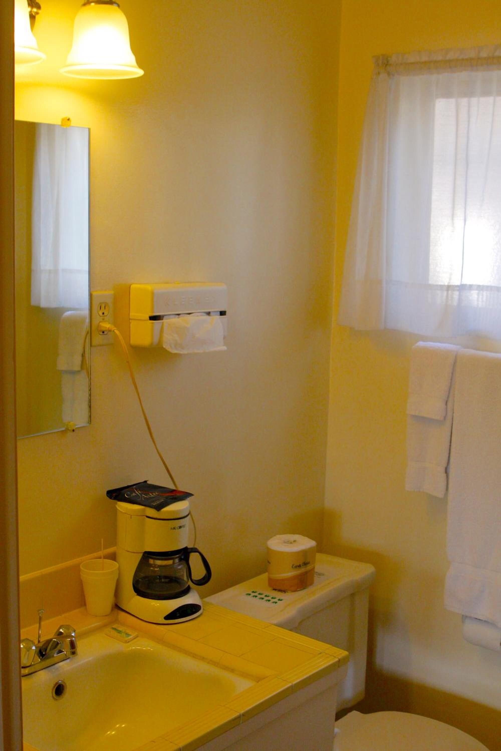 Casa de banho com lavatório, máquina de café, sanita e porta-toalhas.