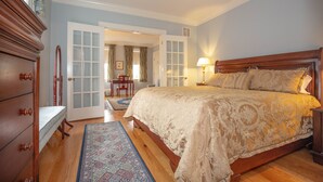 Quarto com uma cama grande, cómoda de madeira e porta que dá para outro espaço.