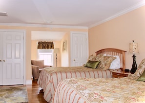 Quarto com cama grande, uma cadeira, abajur e porta para outro cômodo.