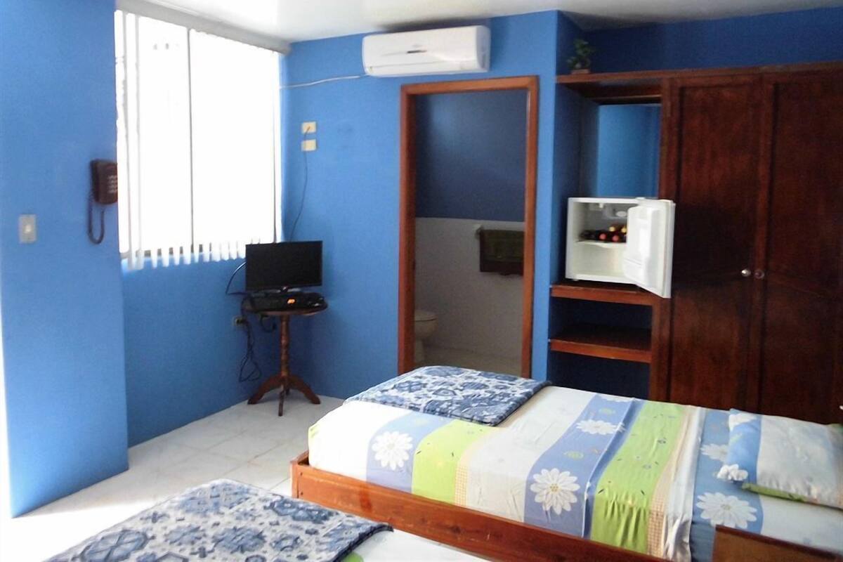 Quarto com cama, guarda-roupa, escrivaninha com computador e ar condicionado.