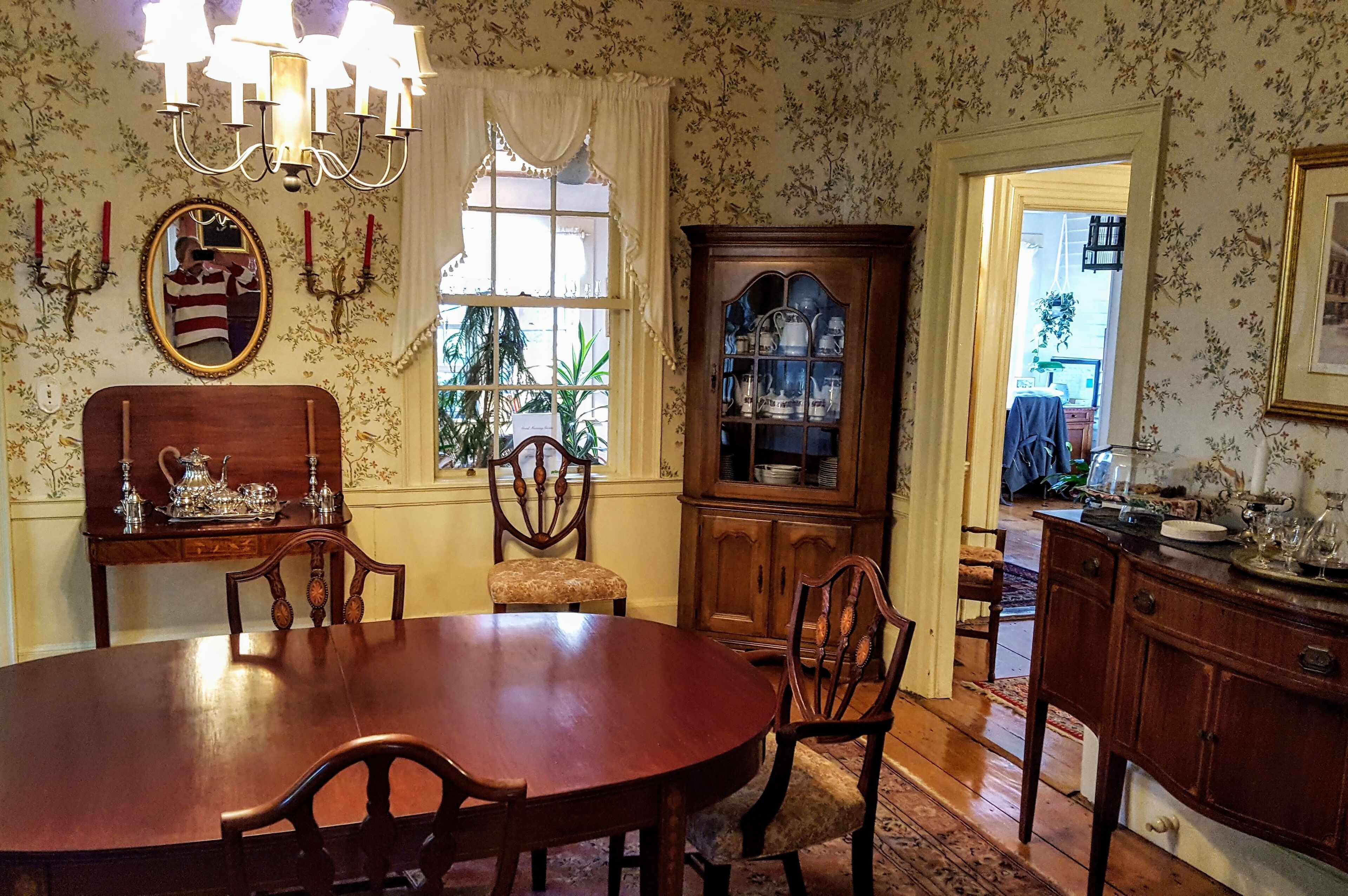 Uma sala de jantar com uma mesa e cadeiras de madeira, um candelabro e um aparador com portas de vidro.