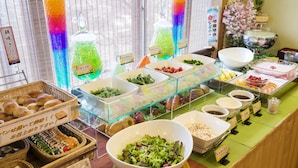 Buffet com diversos alimentos e bebidas, incluindo saladas, frutas e refrigerantes.