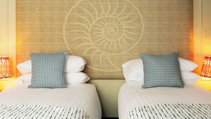 Quarto de hotel com duas camas, almofadas estampadas, um mural grande na parede e abajures laterais.