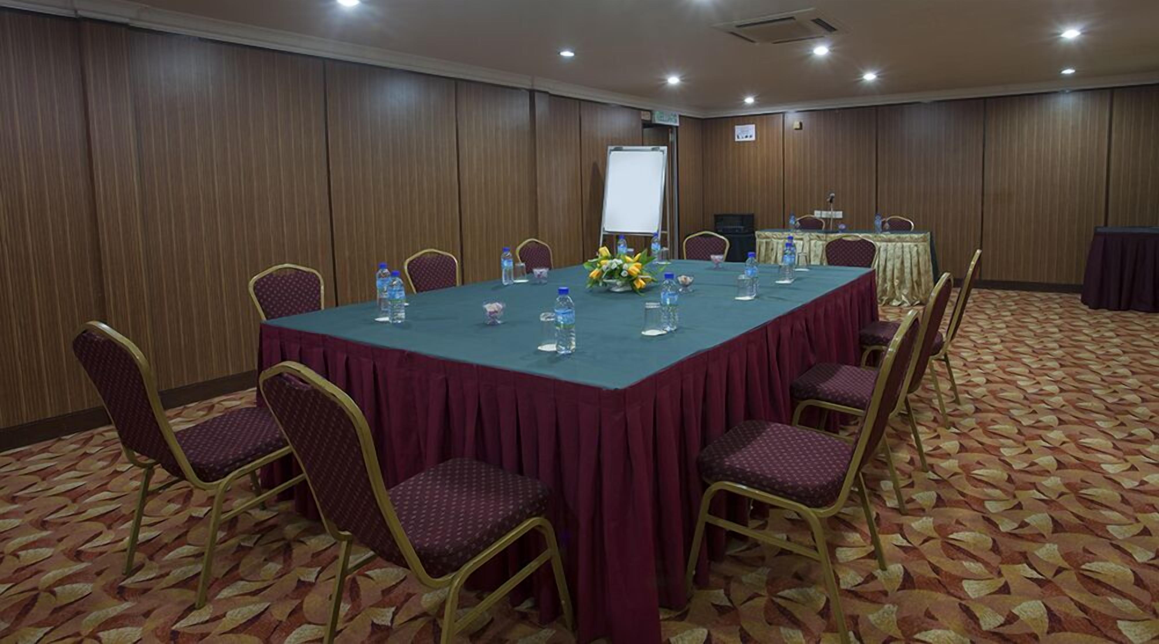 Uma sala de conferência com uma mesa comprida, cadeiras, garrafas de água e um quadro branco.