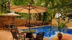 Uma área de piscina ao ar livre com uma parede de tijolos, uma mesa com cadeiras e um grande guarda-sol.