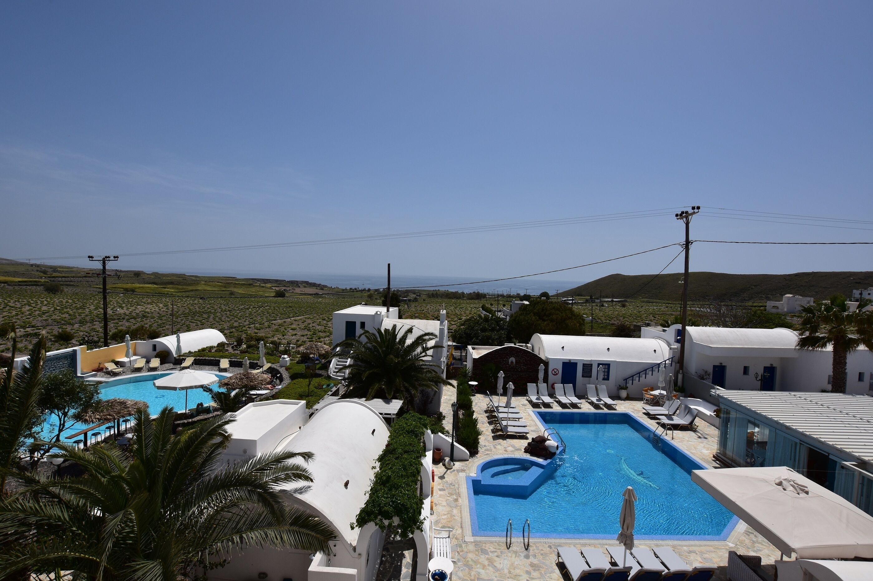 Um resort com uma grande piscina, edifícios brancos e vista para a paisagem.