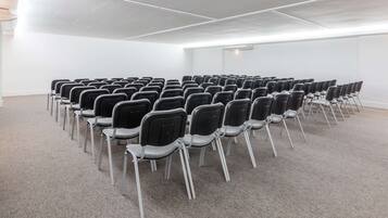 Uma sala de conferências com fileiras de cadeiras pretas e piso coberto por carpete.