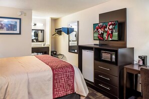 Quarto de hotel com cama, televisão, micro-ondas, cafeteira e escrivaninha com gavetas.