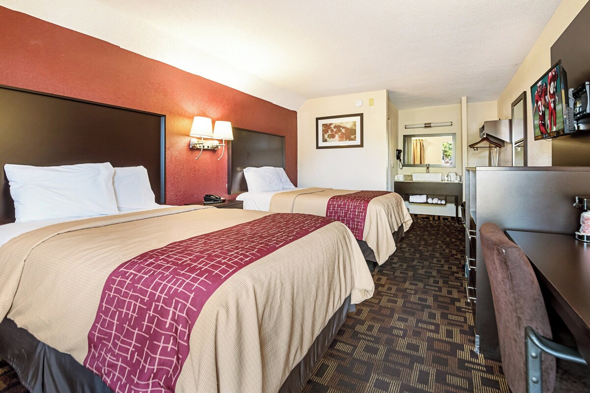 Quarto de hotel com duas camas, uma mesa, uma cadeira, banheiro e televisão.