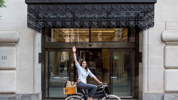 Uma pessoa de bicicleta em frente a um edifício com uma grande entrada em arco e detalhada estrutura metálica.