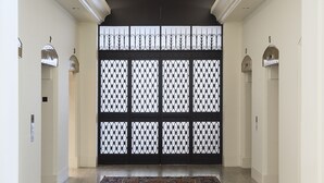 Um corredor amplo com divisória preta e branca estampada, paredes em tons claros e tapete decorado no chão.