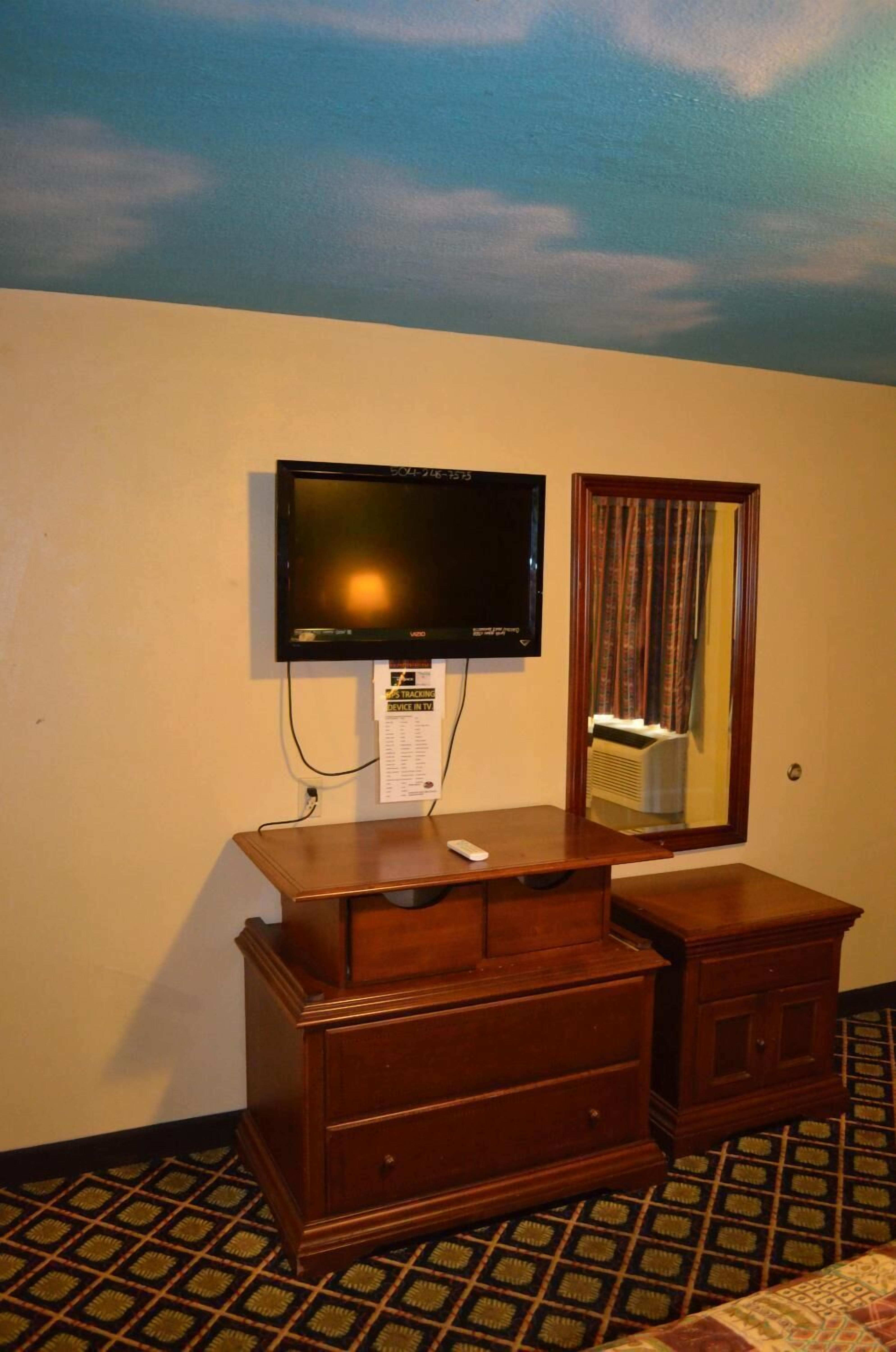 Quarto de hotel com cómoda de madeira, televisão de tela plana na parede e janela com cortinas.