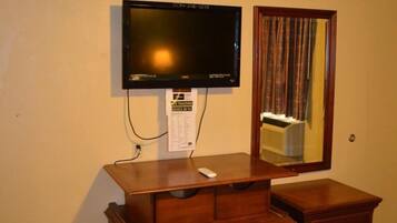 Quarto de hotel com cómoda de madeira, televisão de tela plana na parede e janela com cortinas.
