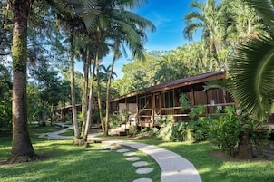 Um resort tropical com um edifício de madeira, um caminho de pedra e vegetação exuberante.