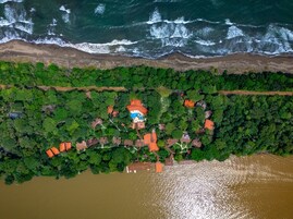 Vista aérea de uma propriedade à beira-mar, com piscina, cercada por vegetação densa e uma praia de areia.