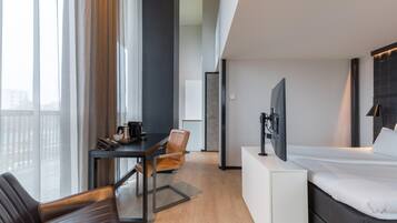 Quarto de hotel moderno com cama, escrivaninha, cadeira e televisão.