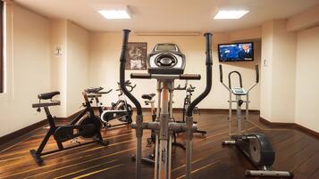 Academia com diversos aparelhos de ginástica, incluindo esteiras e bicicletas ergométricas, dispostos numa sala ampla com piso de madeira.