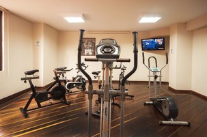 Academia com diversos aparelhos de ginástica, incluindo esteiras e bicicletas ergométricas, dispostos numa sala ampla com piso de madeira.