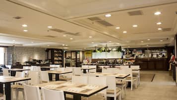 Um restaurante amplo com várias mesas e cadeiras, um balcão com máquina de café e um painel de menu visível.