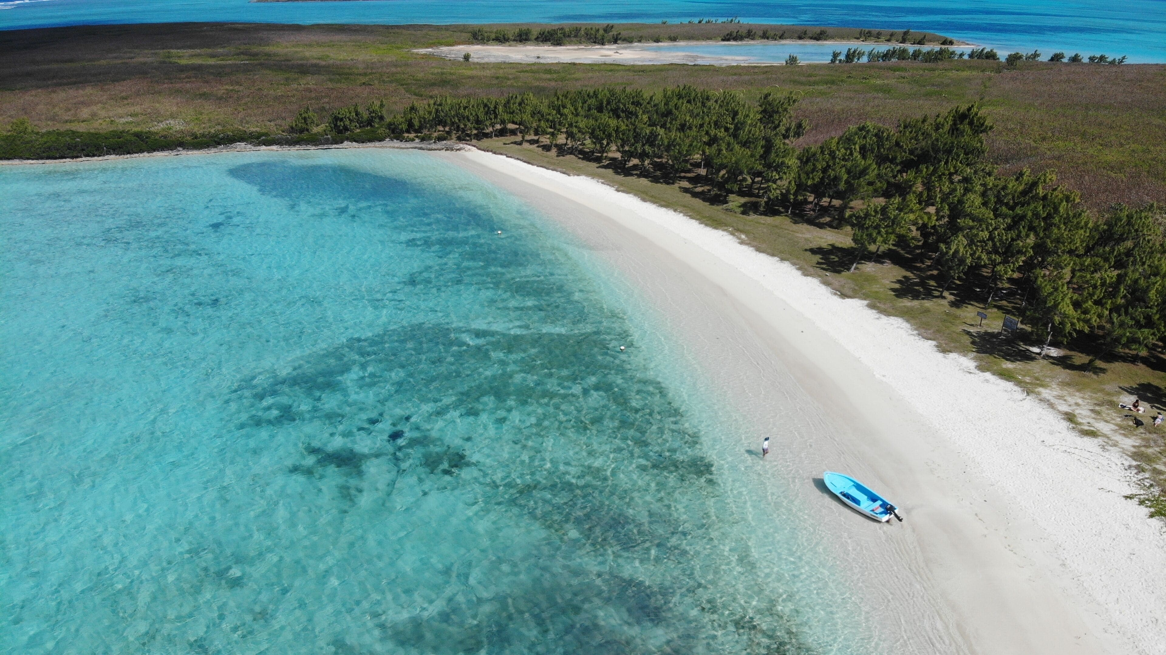 Vista aérea de uma praia com águas turquesa cristalinas, areal arenoso e um pequeno barco na areia.
