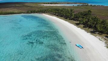 Vista aérea de uma praia com águas turquesa cristalinas, areal arenoso e um pequeno barco na areia.