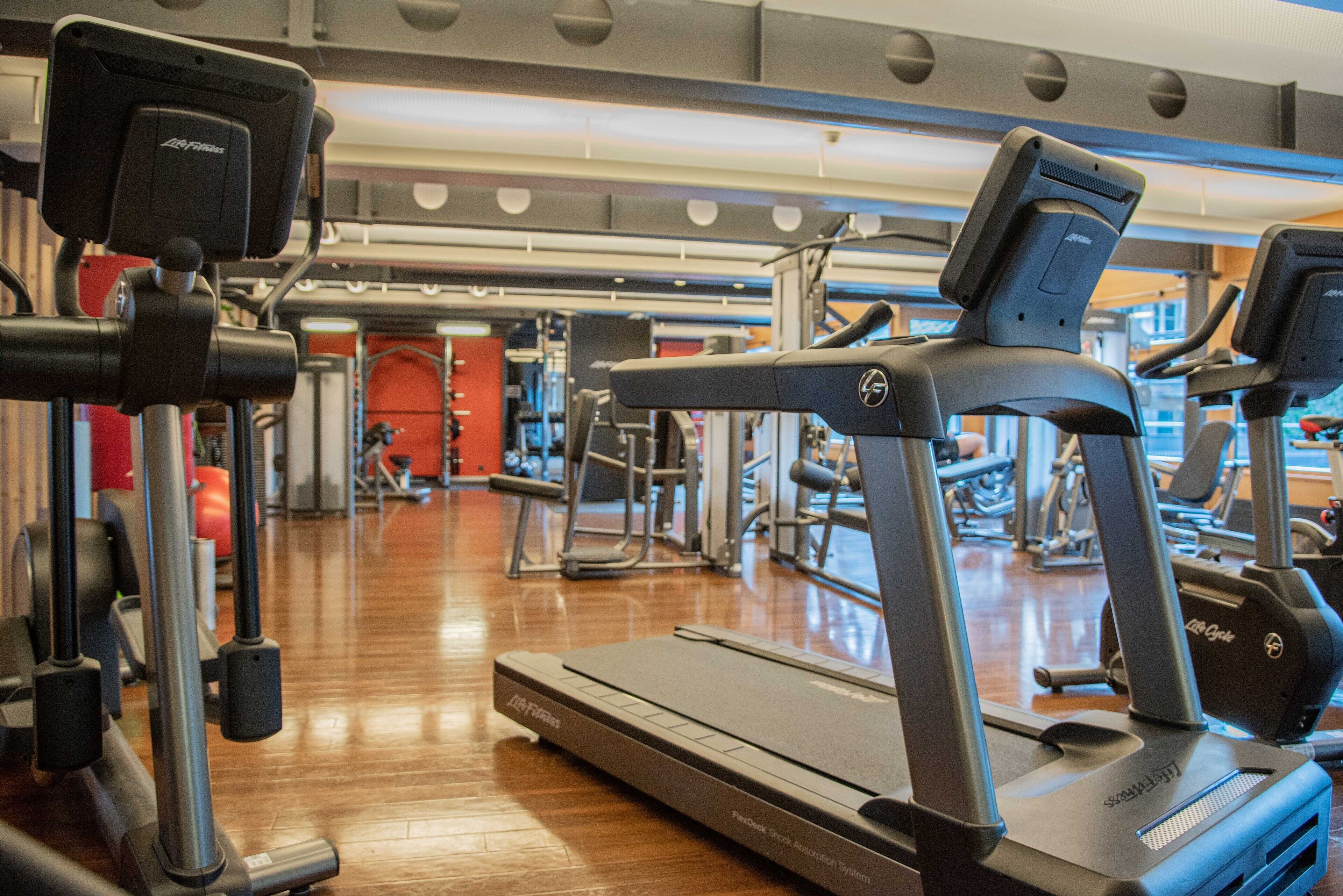 Academia com esteiras, máquinas de musculação e espelho.