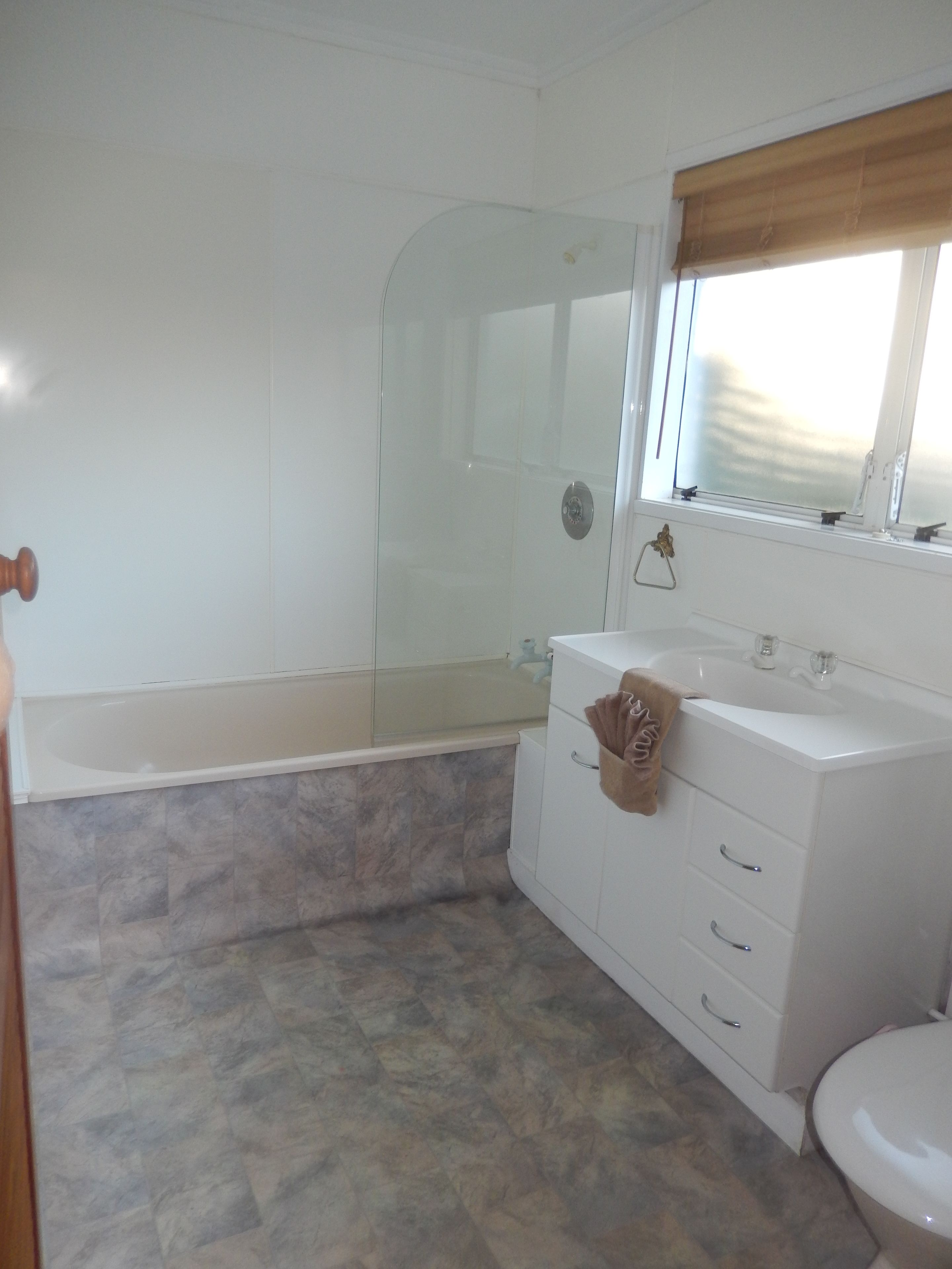 Casa de banho com chuveiro em cabine de vidro, lavatório branco e sanita.