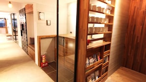 Um corredor com uma estante de madeira, um banco e um pequeno recipiente vermelho.