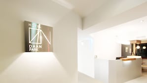 Uma área de recepção de hotel com design moderno, balcão de atendimento e placa indicando o nome e a localização do hotel.
