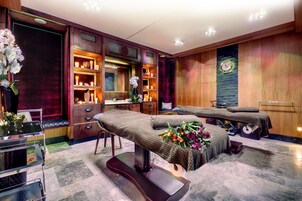 Sala de spa com duas macas de tratamento, um balcão de recepção e uma estante com velas e objetos decorativos.